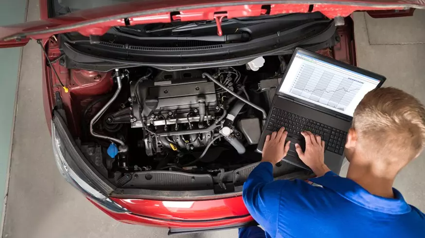 Mechaniker, der Automotor mit Hilfe des Laptops untersucht