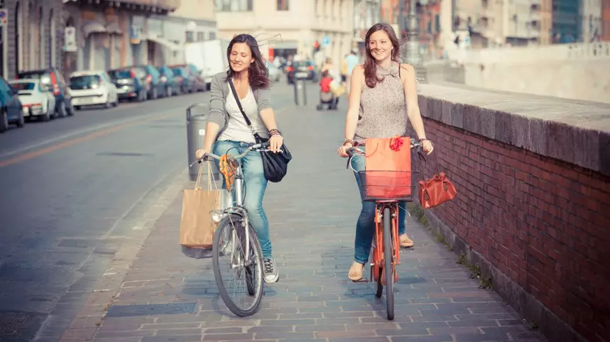 Twee mooie vrouwen die in de stad met fietsen en tassen lopen