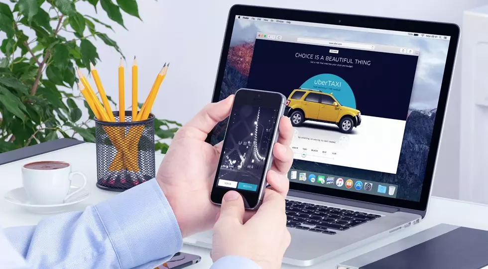 Ohun elo Uber lori ifihan ipad ni awọn ọwọ ati oju opo wẹẹbu Uber lori